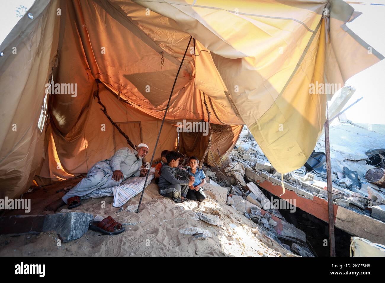 Palestinians sit in a makeshift tent amid the rubble of their houses ...