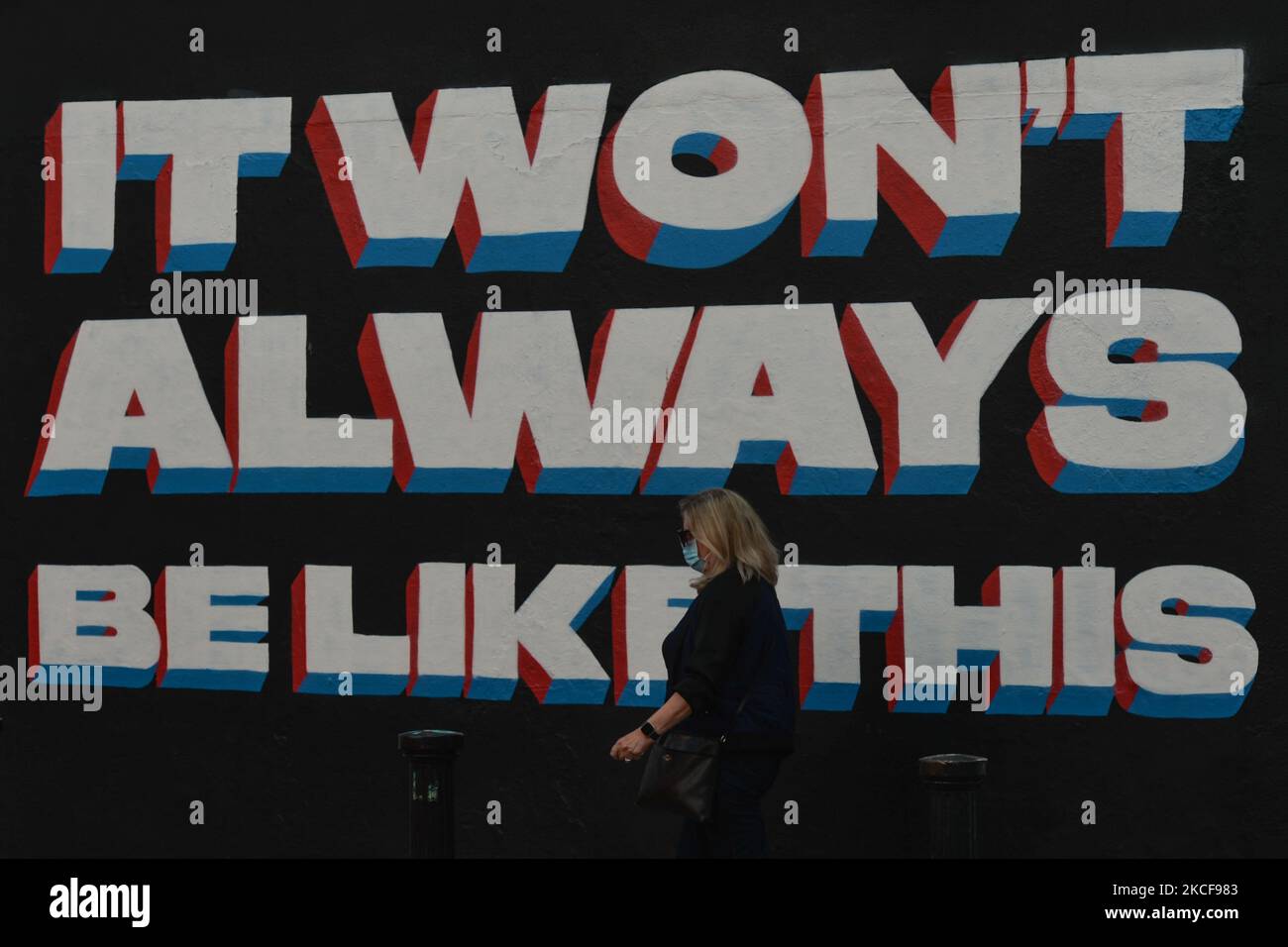 A woman wearing a face mask walks past a mural with the words 'IT WON'T ...