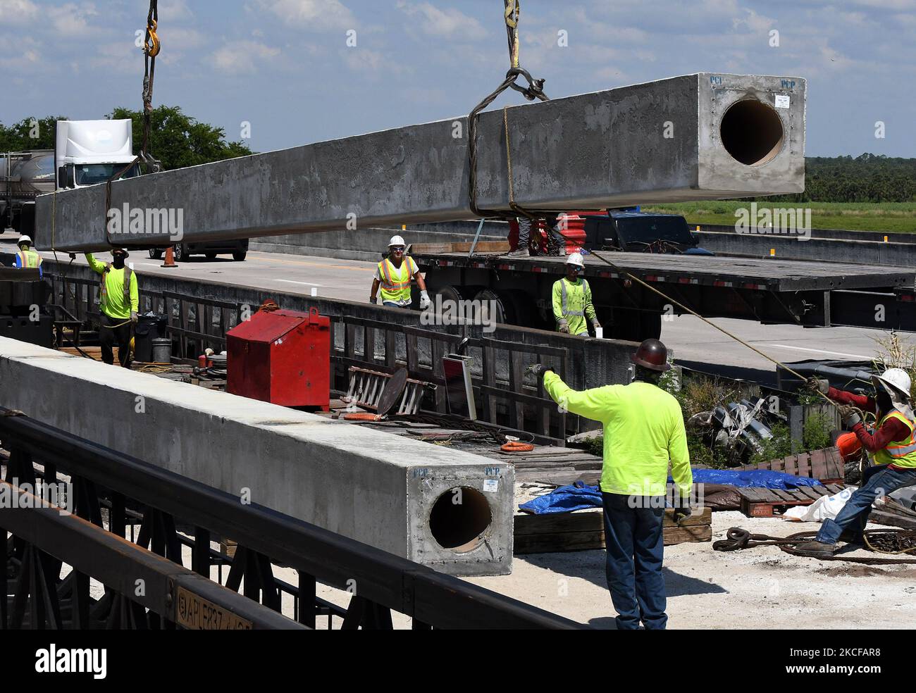 Workers receive piles for a bridge over the St. Johns River as they are ...