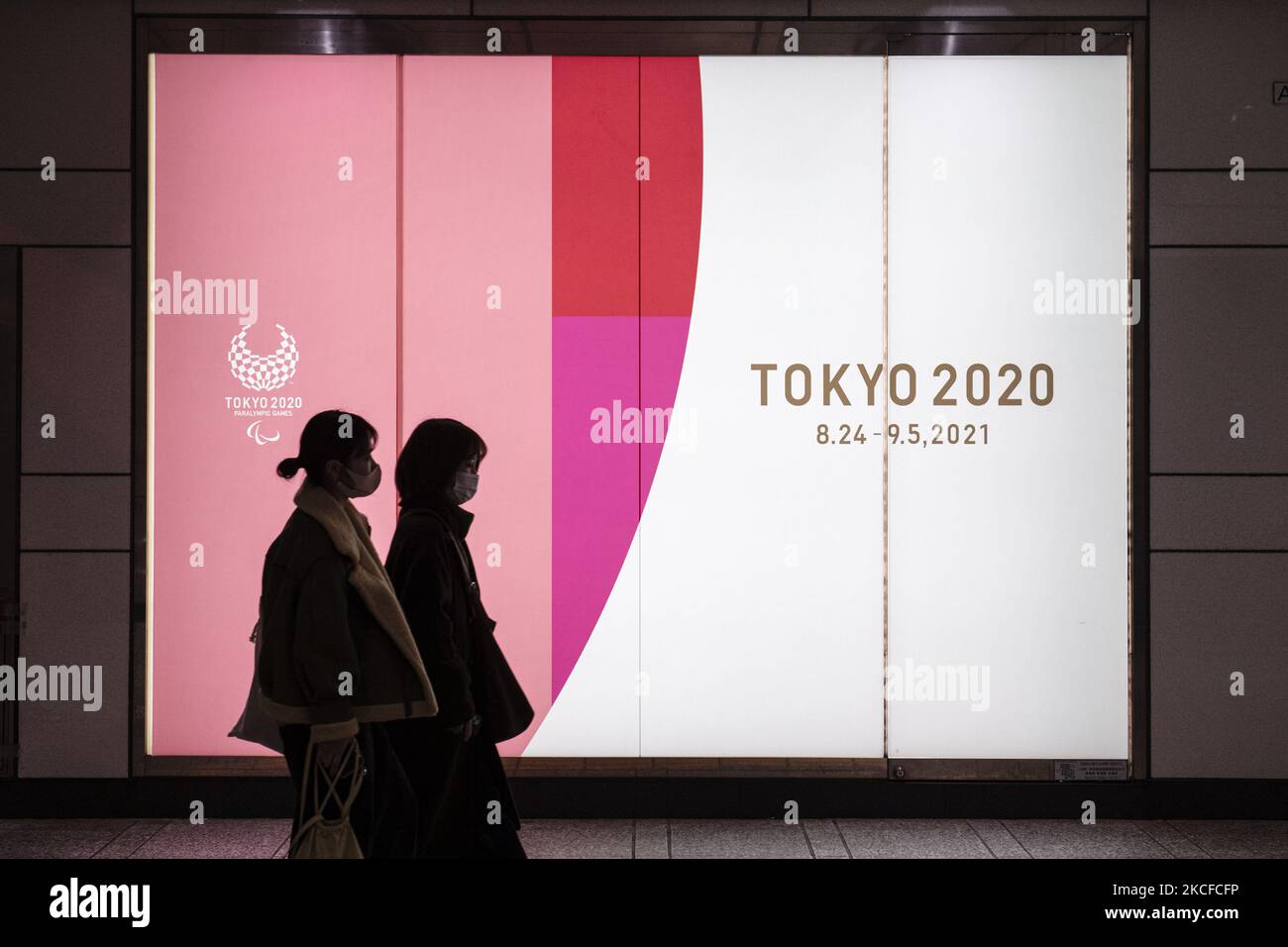 Masked women walk past an electronic sign board for the Paralympic ...