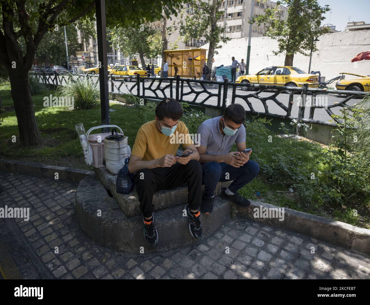 Two Iranian men wearing protective face masks use their smartphones ...