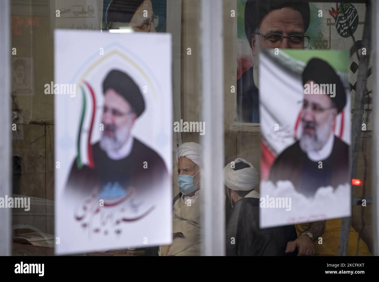 Two Iranian clerics sit behind the electoral posters at a campaign ...
