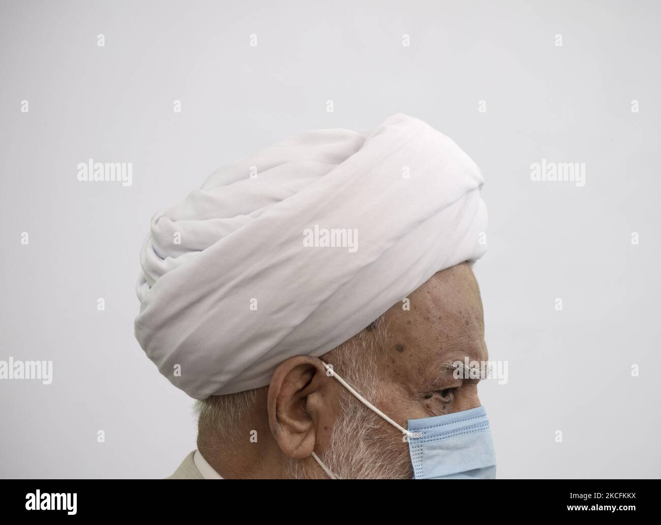 An Iranian cleric wearing a protective face mask looks on while ...