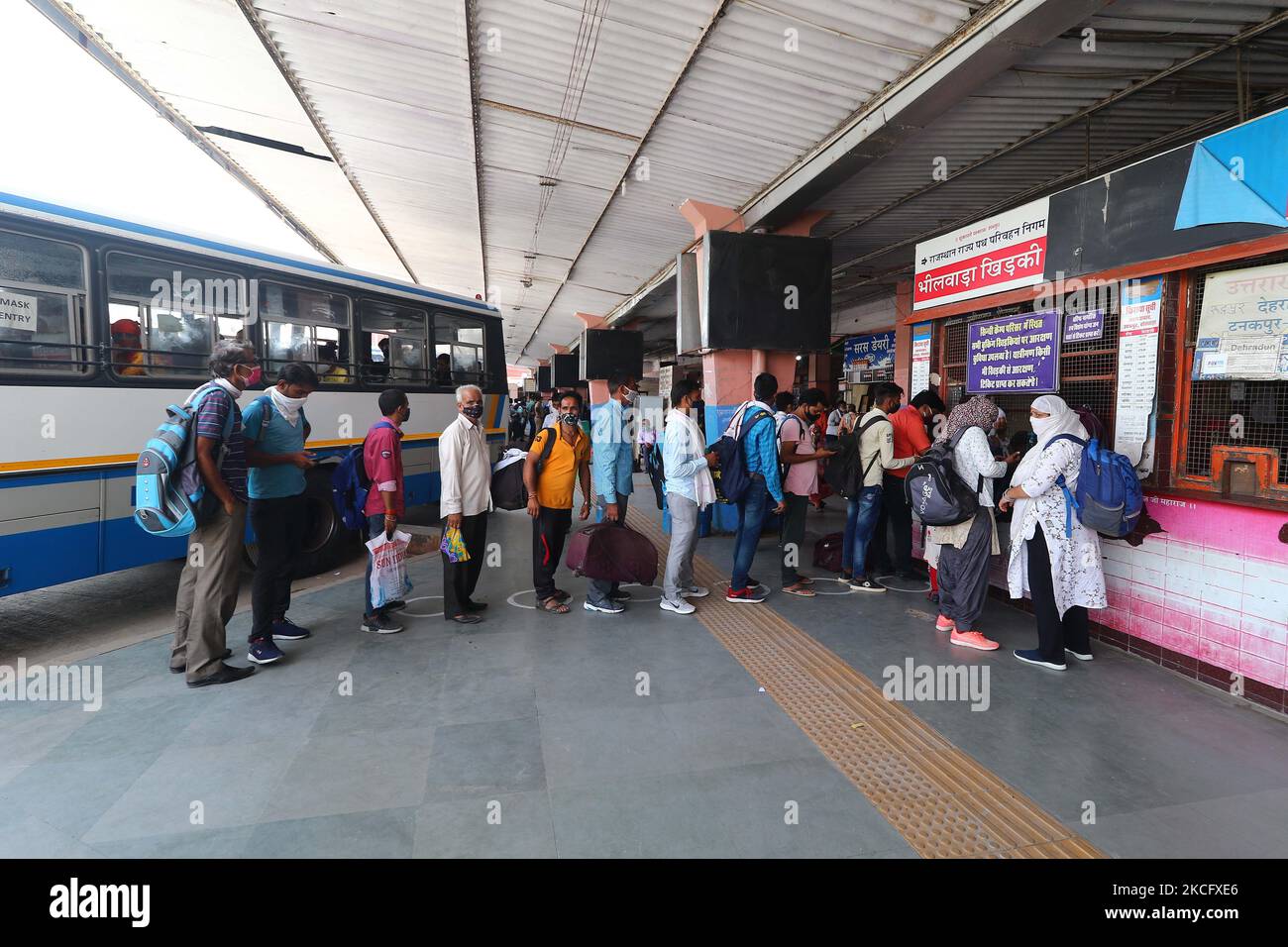 Passengers stand in a queue at a ticket counter to board buses for ...