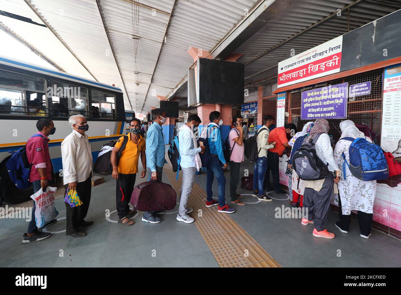 Passengers stand in a queue at a ticket counter to board buses for ...