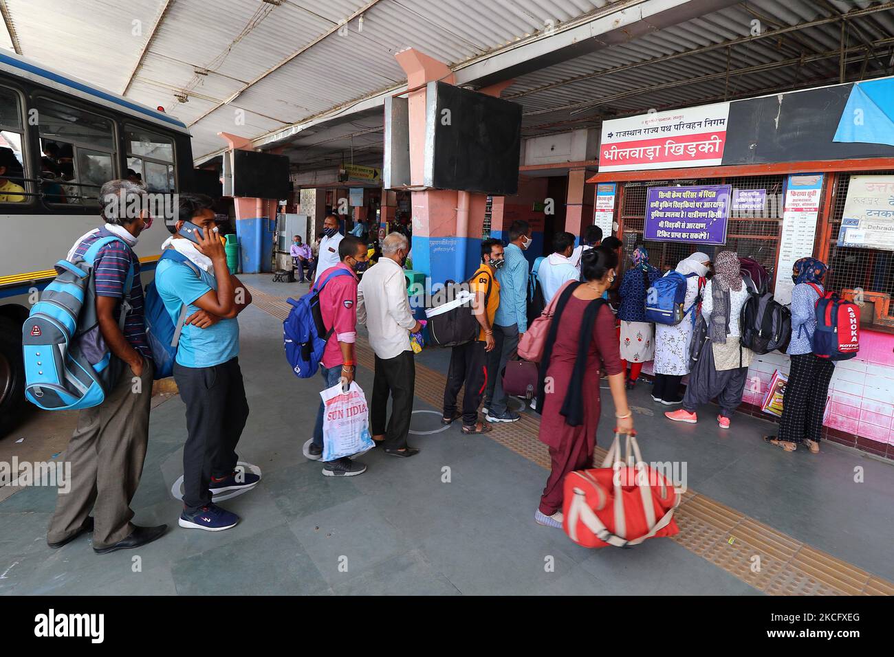 Passengers stand in a queue at a ticket counter to board buses for ...