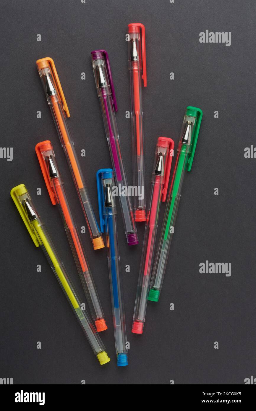 eight colorful pens scattered on black paper surface, school and office ...