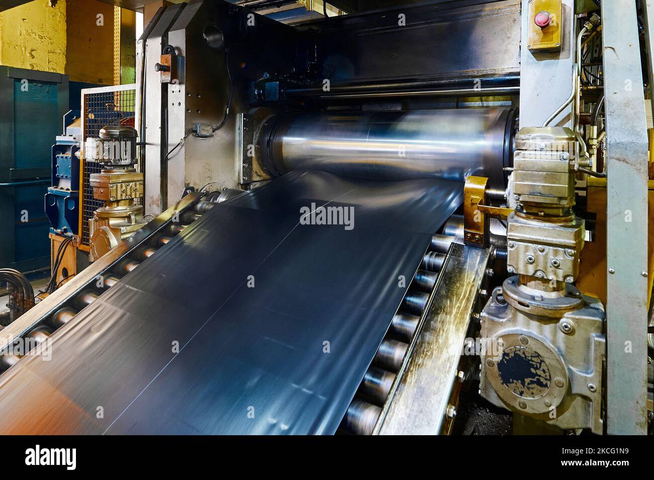 A wide belt of raw rubber compound moves along a roller conveyor. Plant ...