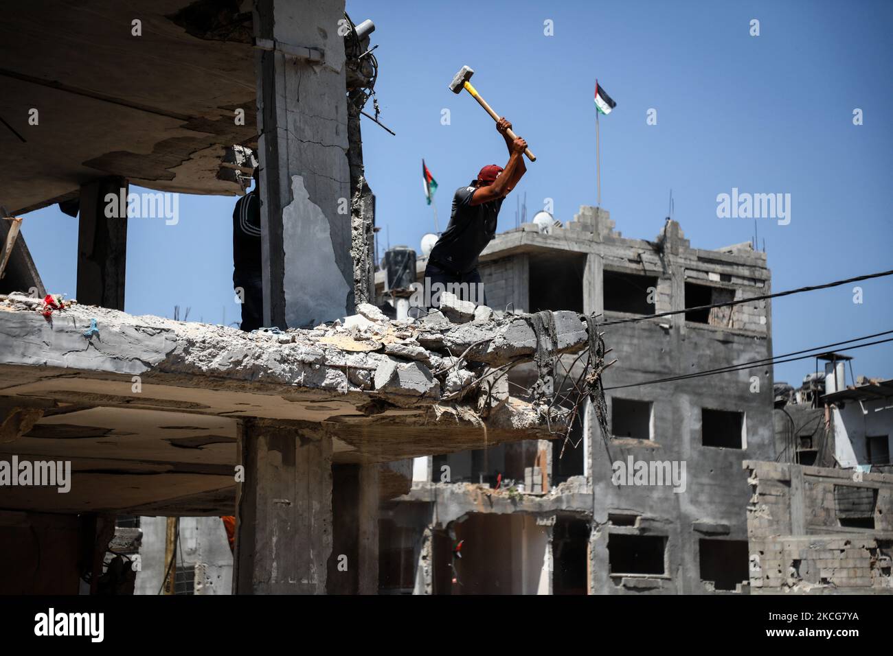 Workers use rudimentary tools to break parts of a building, damaged by ...