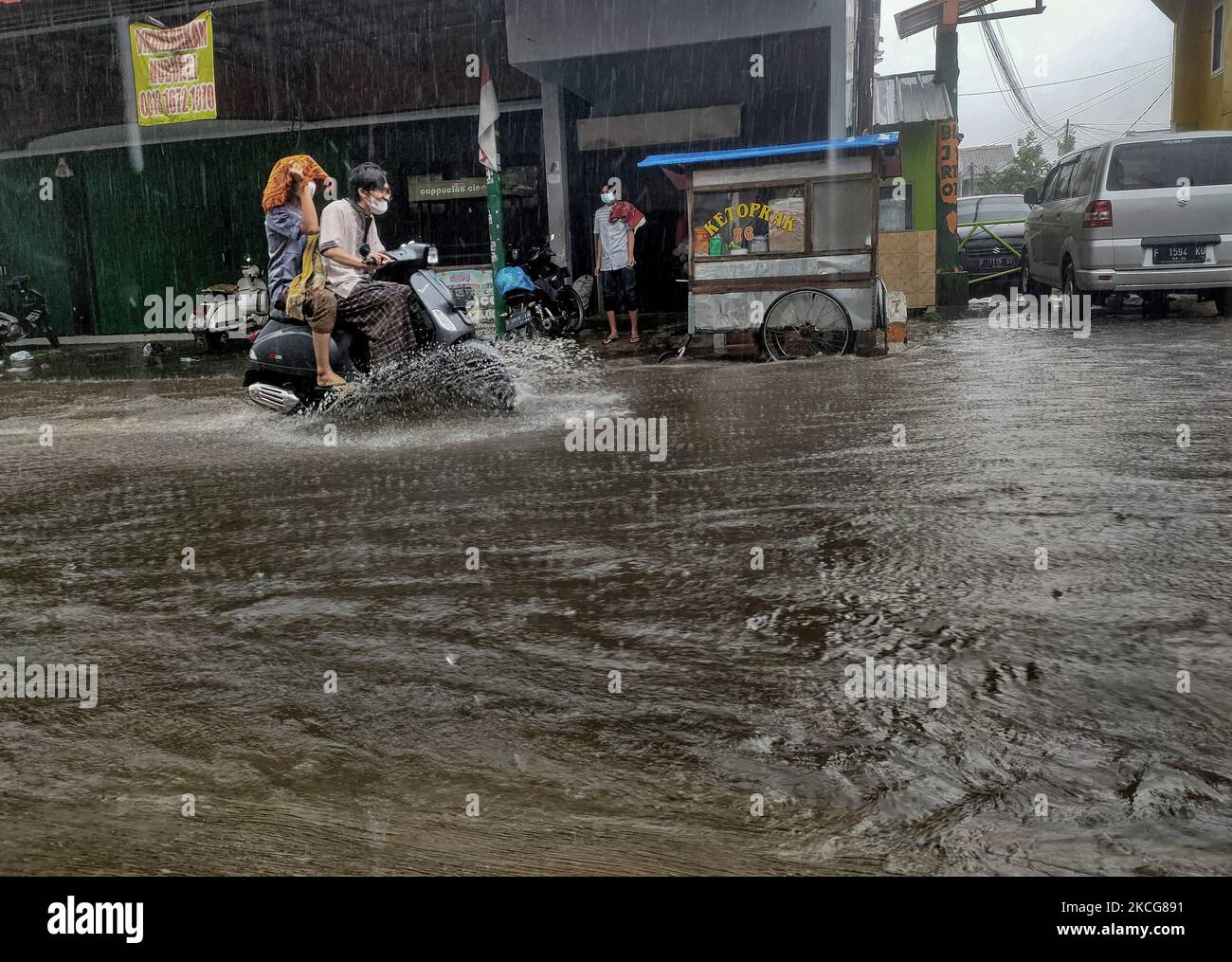 A commuters make their way along a waterlogged street after heavy rains ...