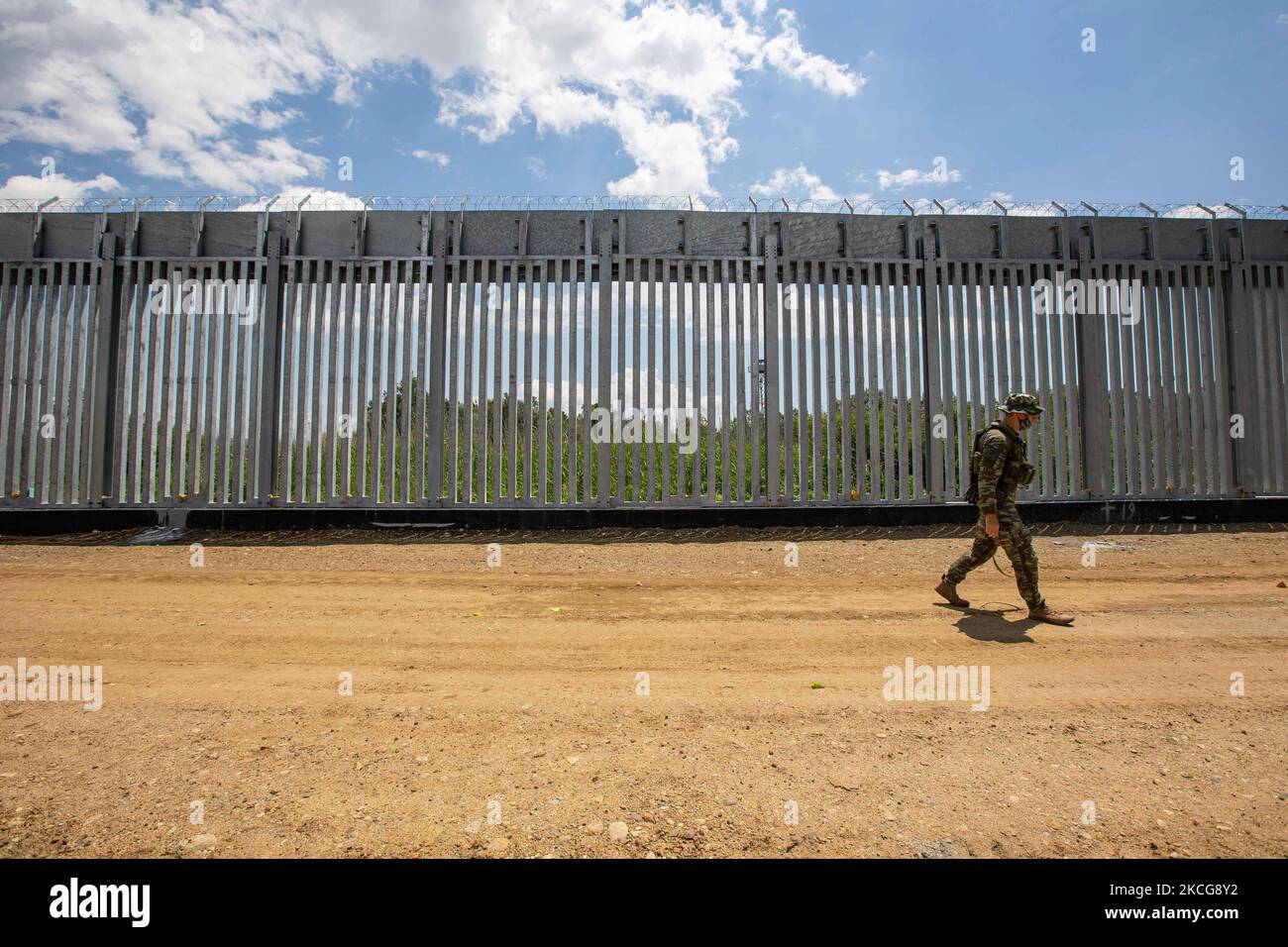 An armed military personnel is patroling along the fence, while there ...