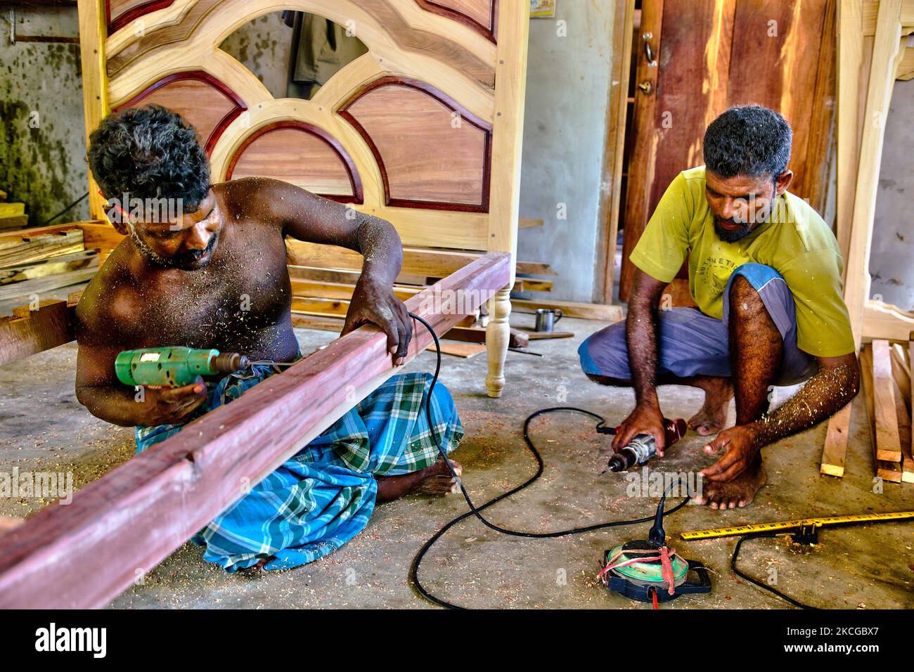 Carpenters construct a fancy wooden bed frame at a small workshop in ...