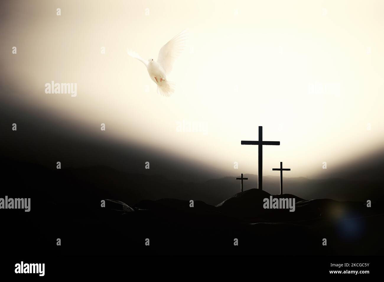 White dove flying over the cross of Jesus and silhouette on bright sky ...