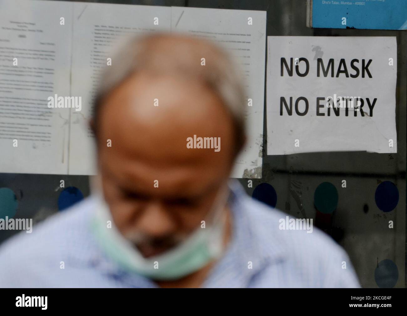 A man without a face mask stands in front of a printed paper as No Mask ...