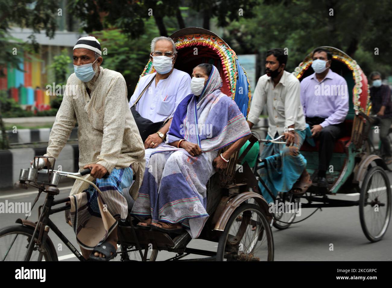 People wear masks as they ride on rickshaws in the early morning during ...