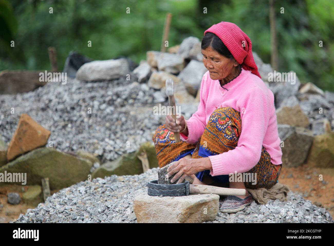 Nepalese woman laborer breaks rocks into gravel with a rubber tool with ...