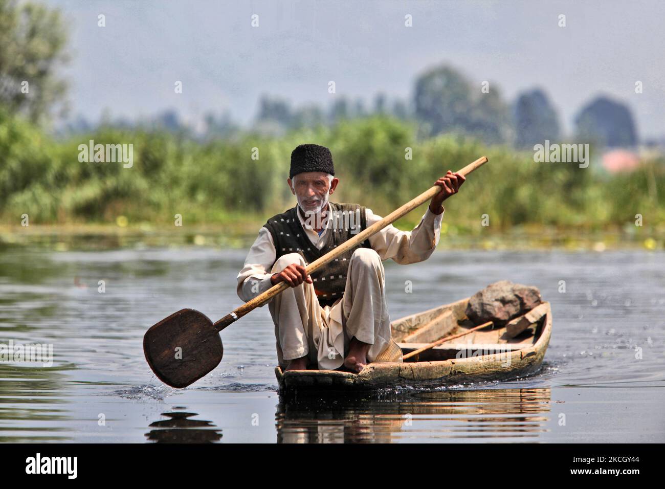 Kashmiri Muslim man travels on a small boat along the backwaters of Dal ...
