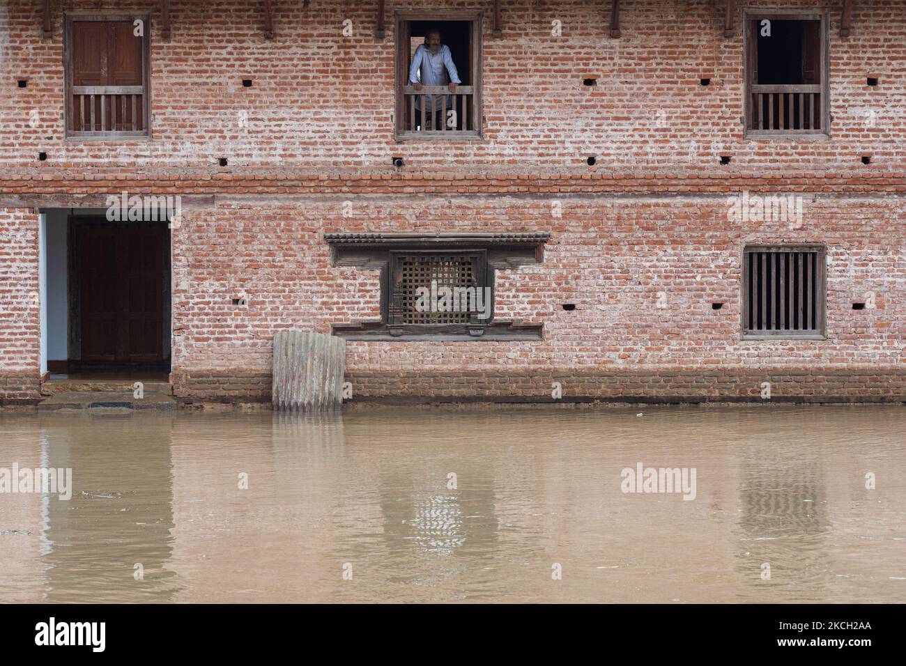 A man looks outside the window of a house at the flood-affected area in ...