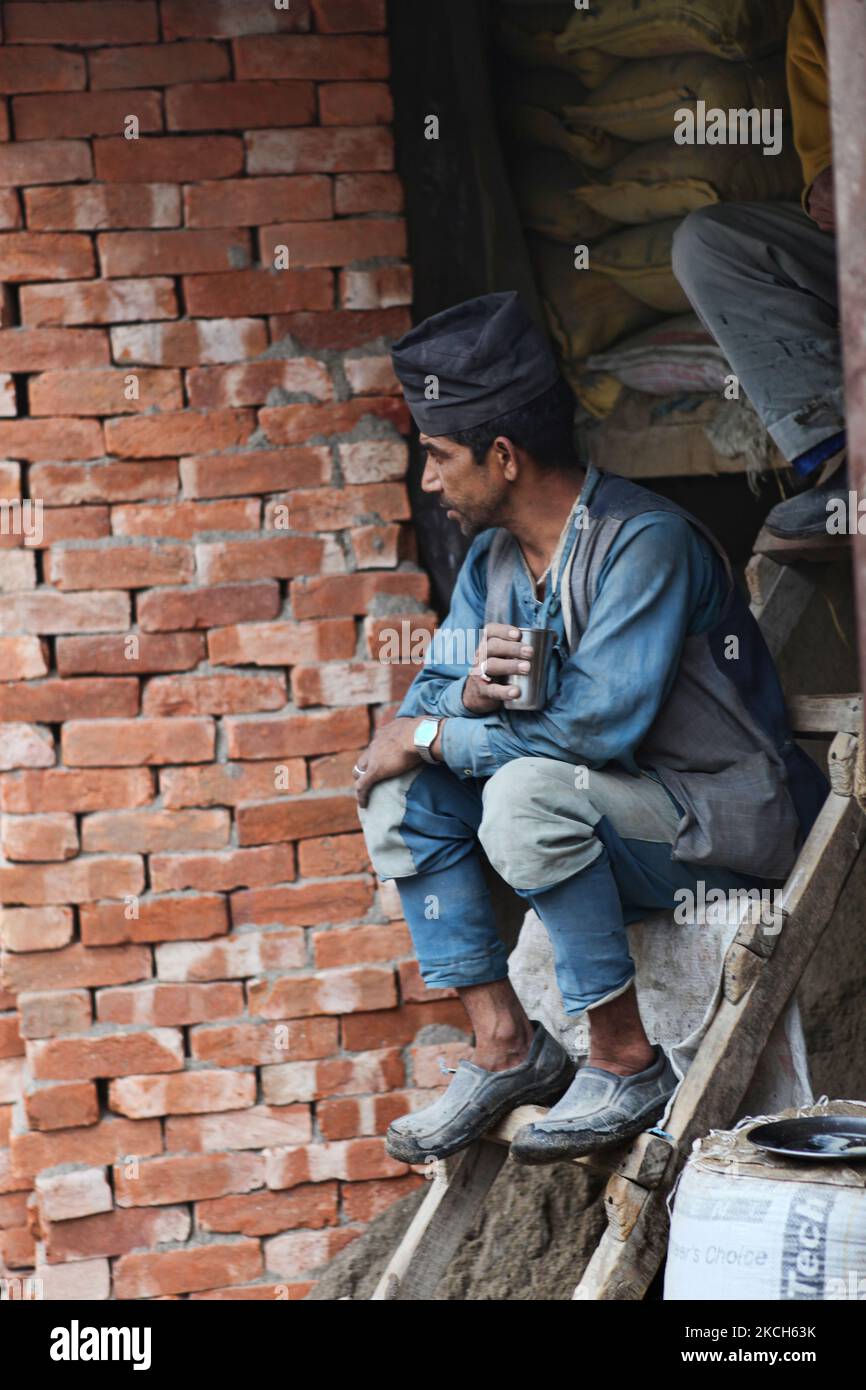 Nepali bricklayer wearing a traditional cap takes a break and drinks a ...