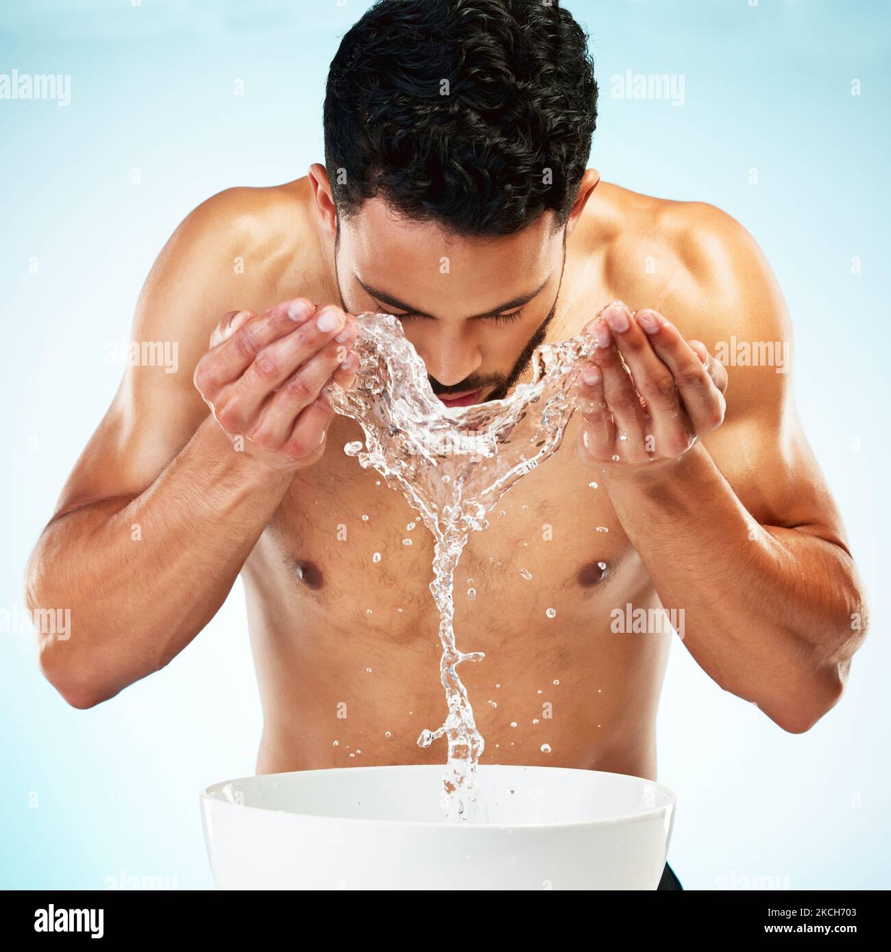 Water splash, studio and man cleaning face in a daily grooming morning routine for healthy ...