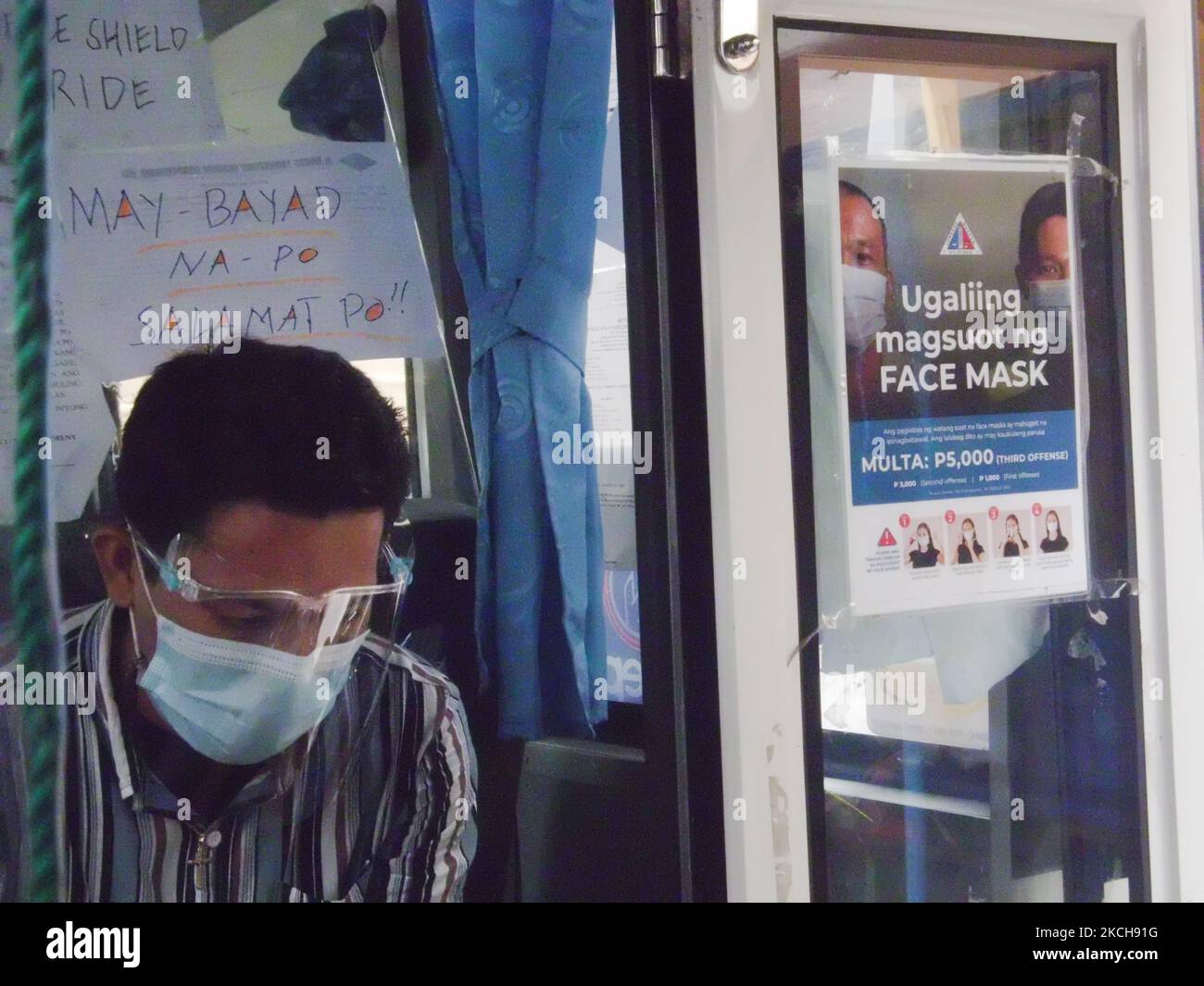 A passenger wearing a face mask and face shield sits next to a door ...