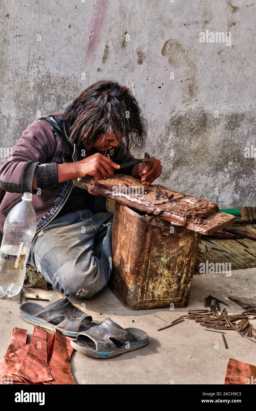 Metal worker uses a chisel to create small designs in a copper sheet at ...