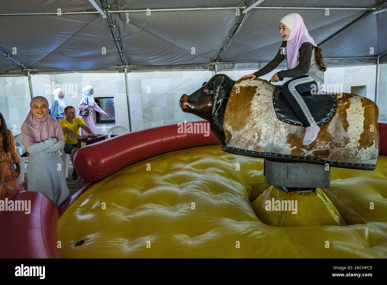 A muslim girl rides a mechanic bull for playing during the celebrations ...