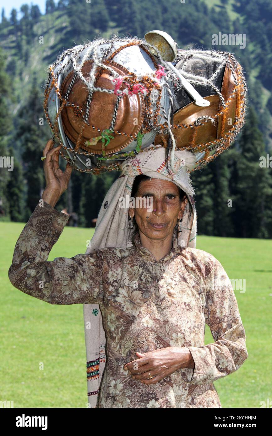 A nomadic Bakharwalli woman carries a large bundle of pots and pans on ...