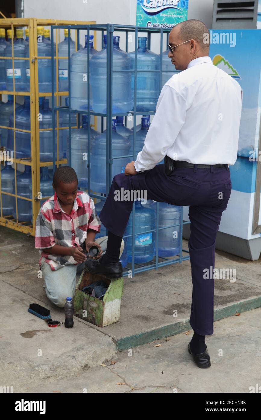 Young boy polishes the shoes of a man along the roadside in La Romana ...