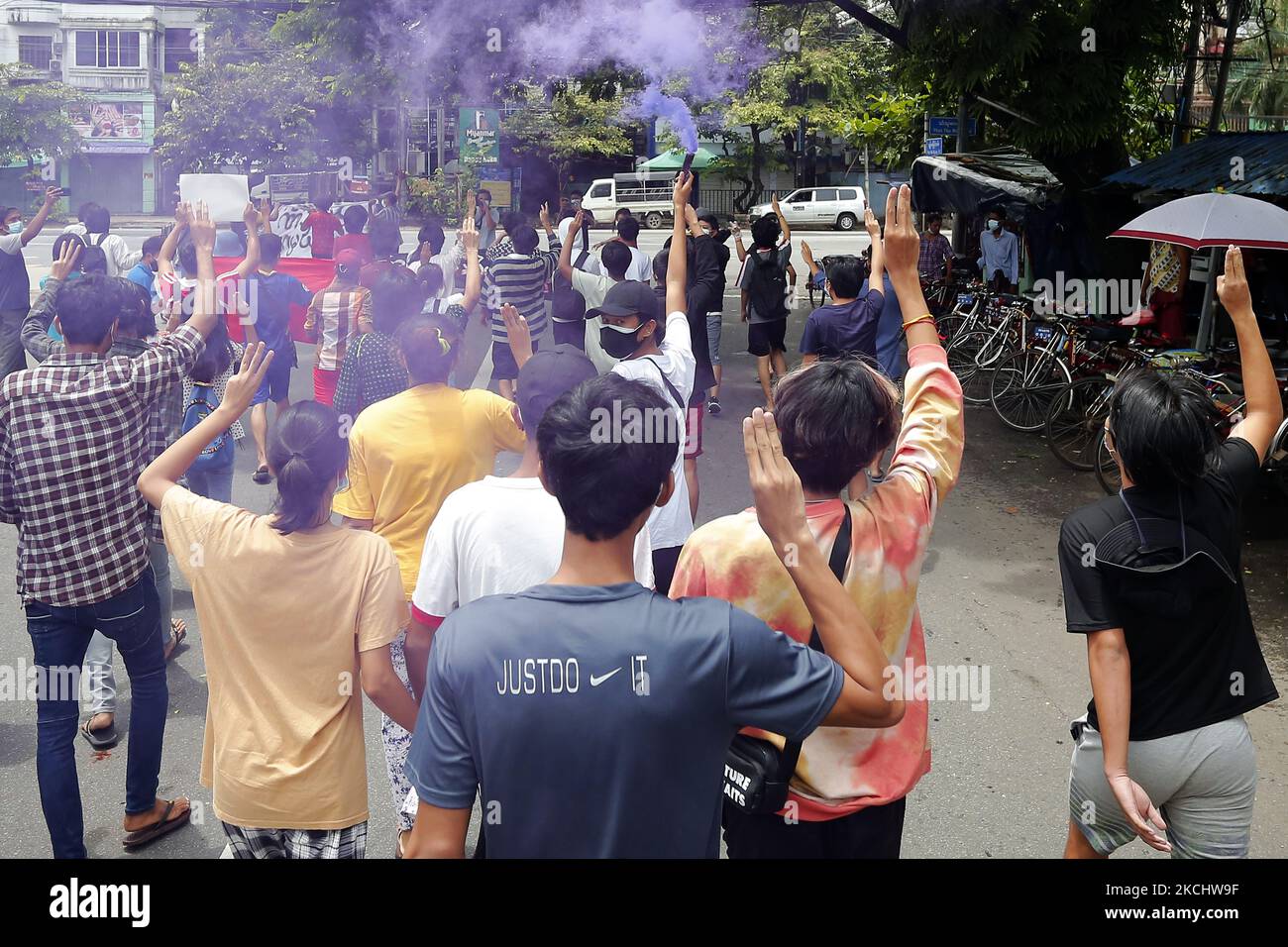 Demonstrators make the defiant three-finger salute and hold flares as ...