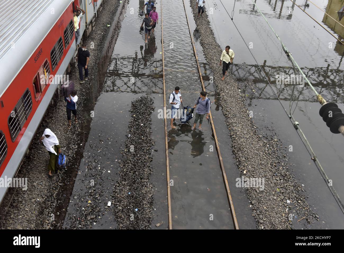 Long distance train passengers walk through the flooded railway tracks ...