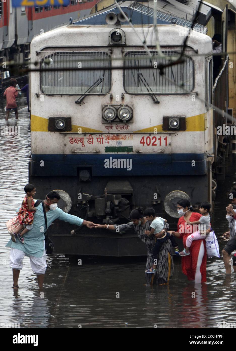 Long distance train passengers walk through the flooded railway tracks due to heavy rainfall in ...