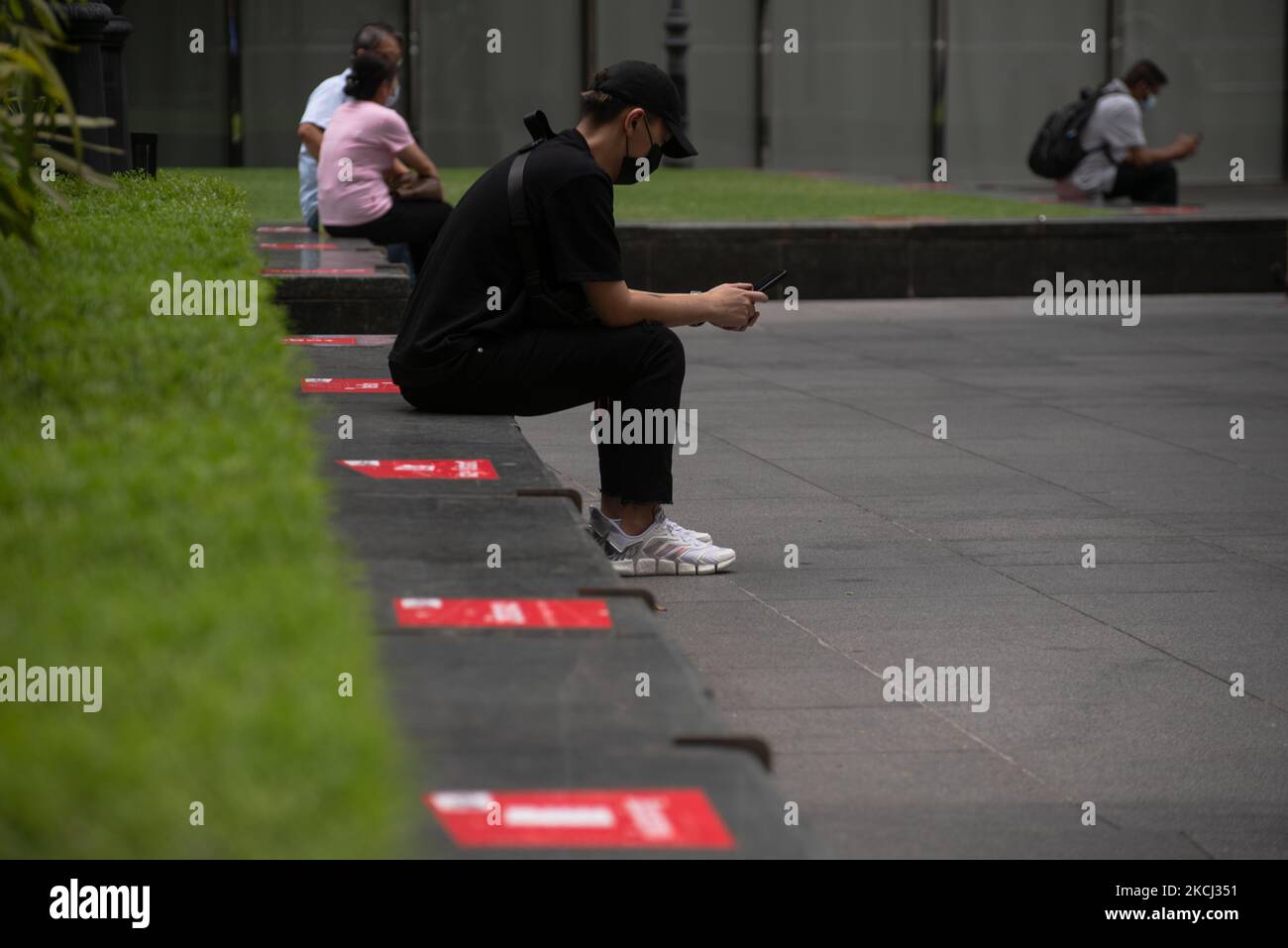 People sit in Singapore's Raffles Place, guided by red stickers on ...