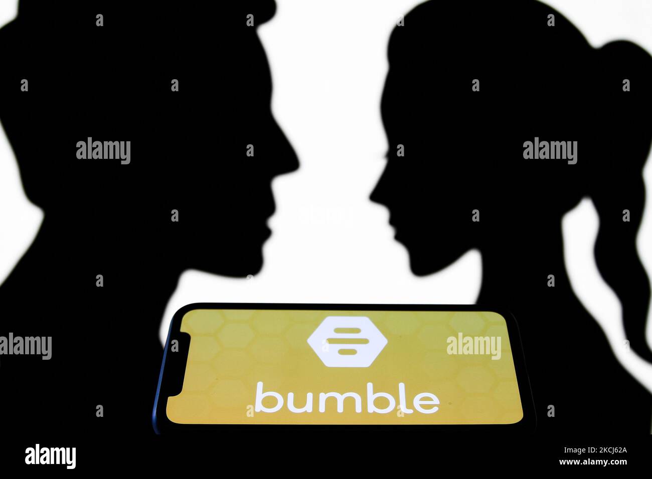 Bumble logo displayed on a phone screen is seen with paper silhouettes ...