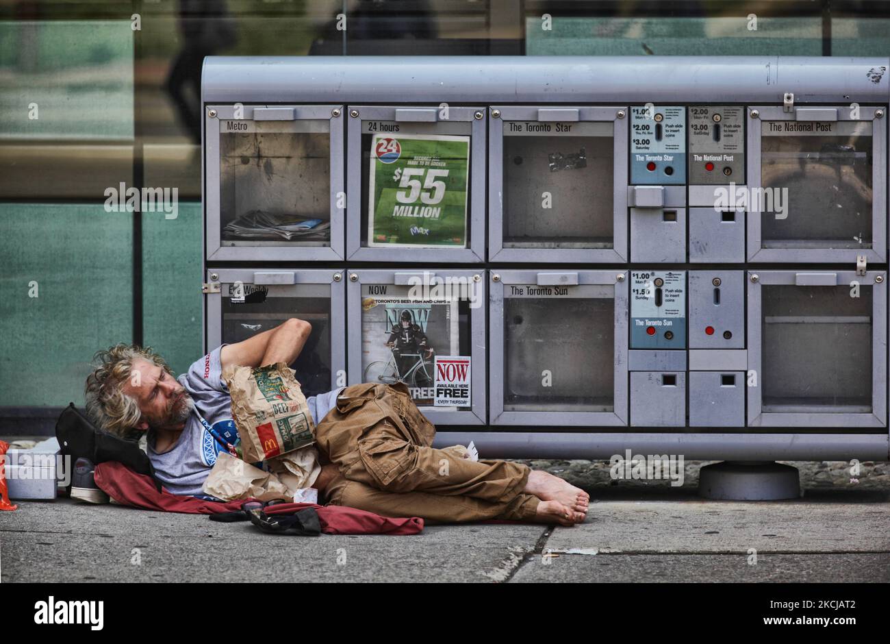 Homeless man rests on the pavement of a busy street in downtown Toronto ...