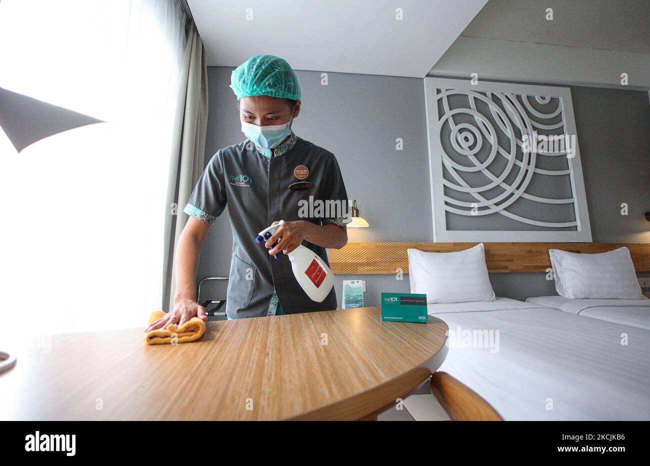 a housekeeping employee wearing face mask clean a table inside a room ...