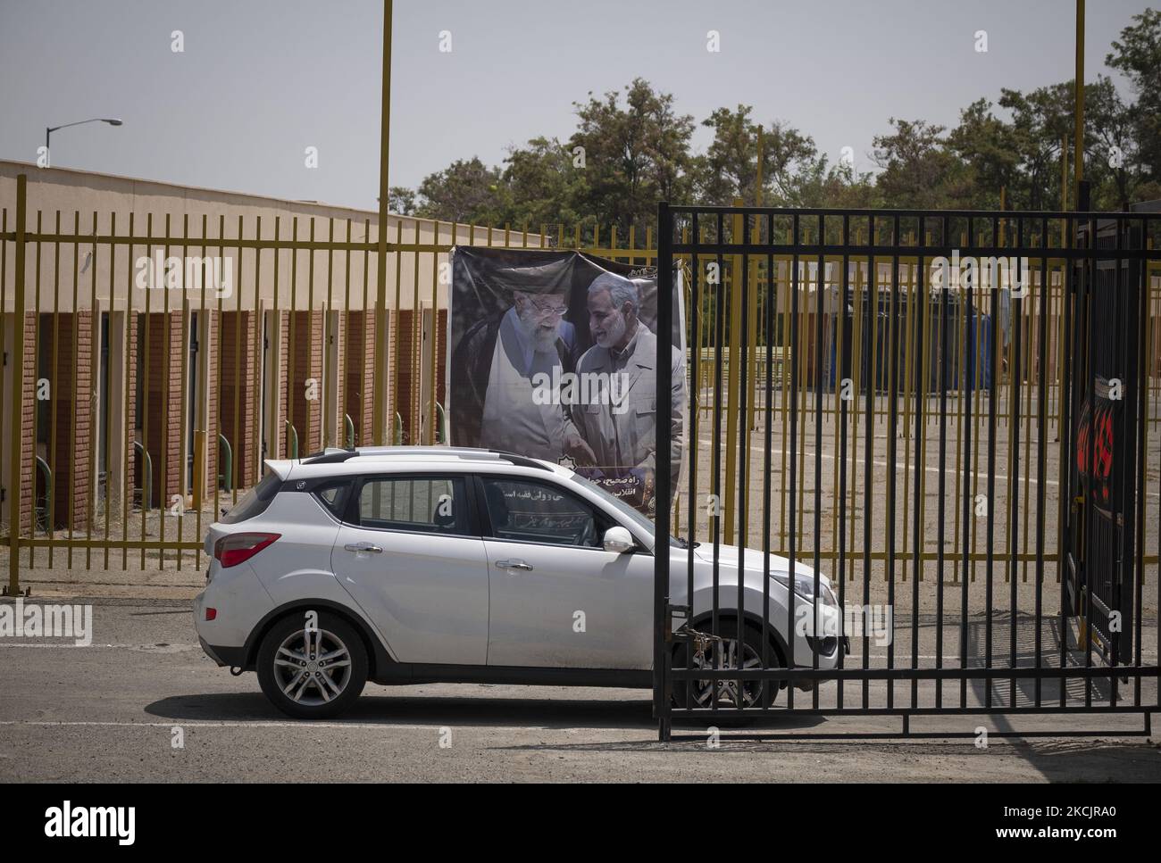 An Iranian man sits at his vehicle in front of a banner with portraits ...