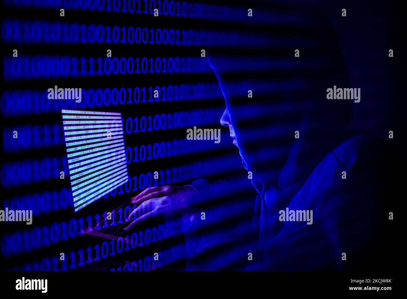 A person dressed as an internet hacker is seen with binary code ...