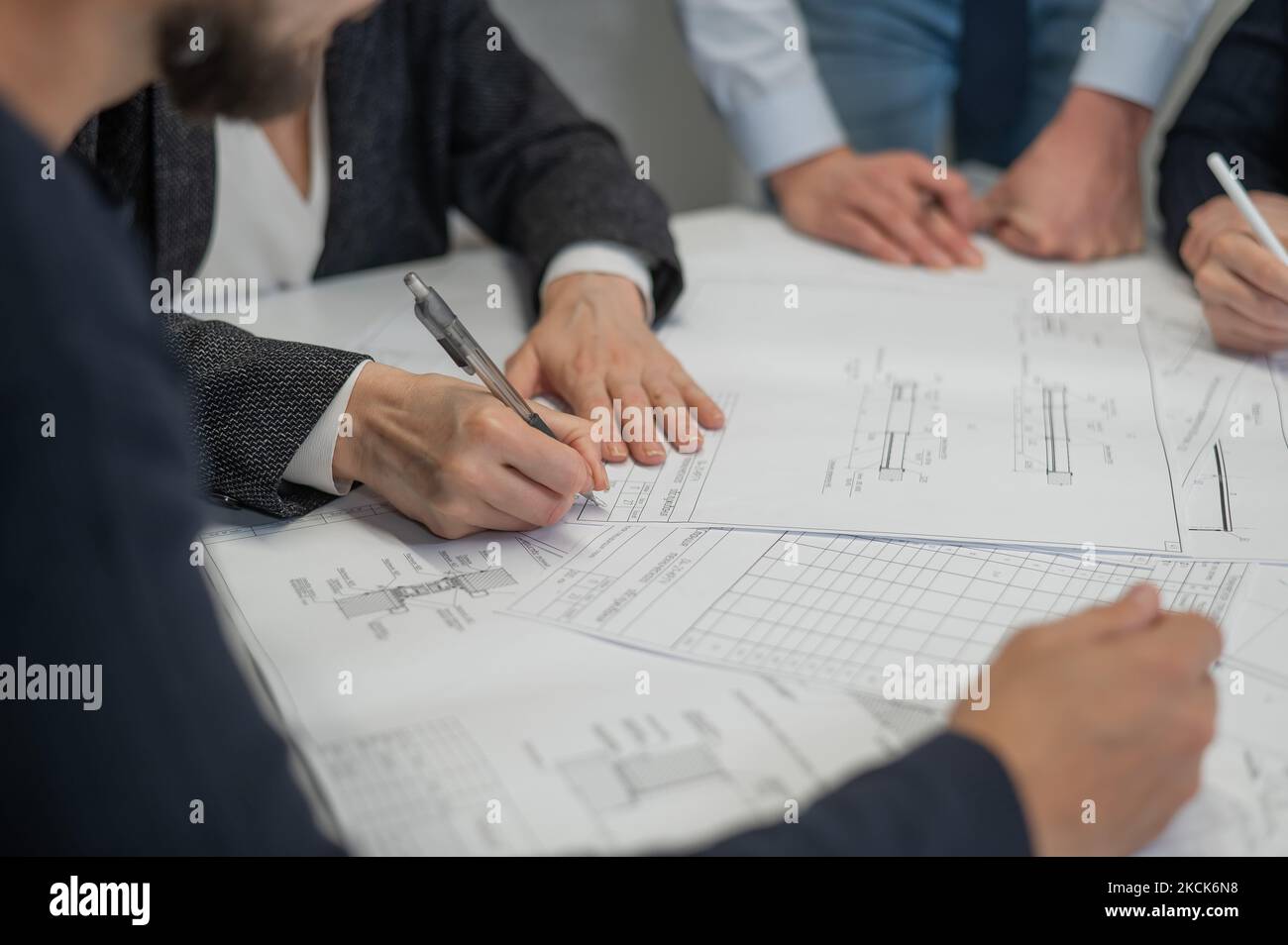 Close-up of the hands of four colleagues with blueprints on the table ...