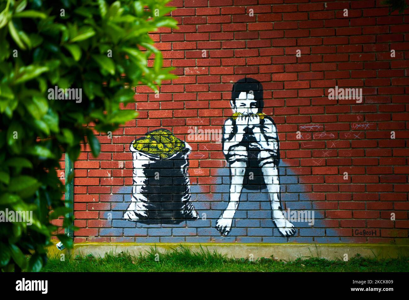 Graffiti drawing on a brick wall. A boy eats corn while sitting near a ...