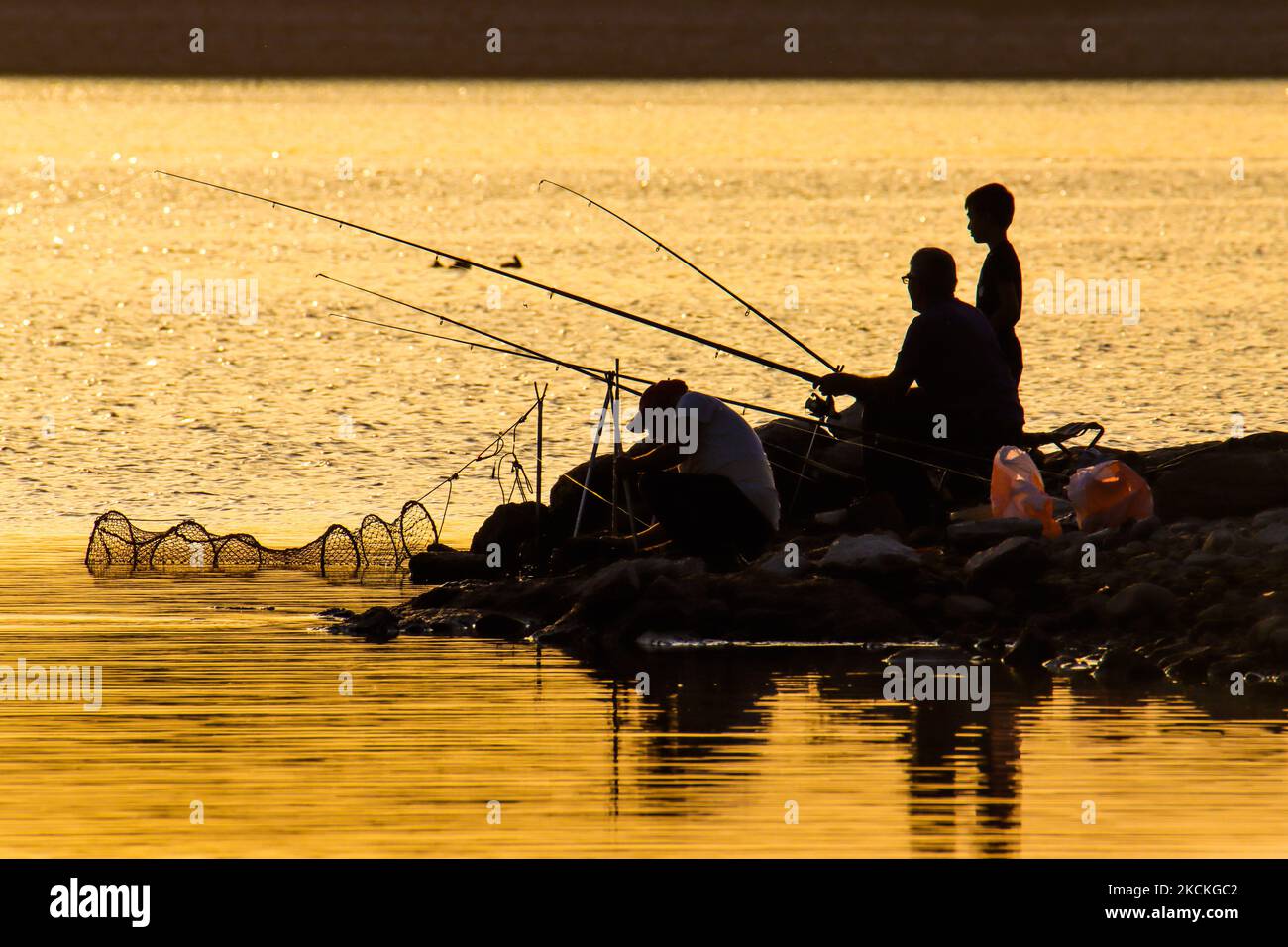 People fishing at the lake early morning, while the sun is reflected on ...