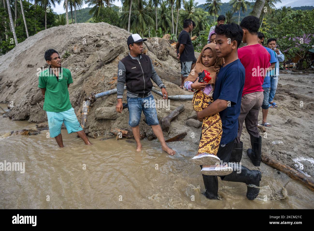 Residents carry children to cross a road covered in water and mud after ...