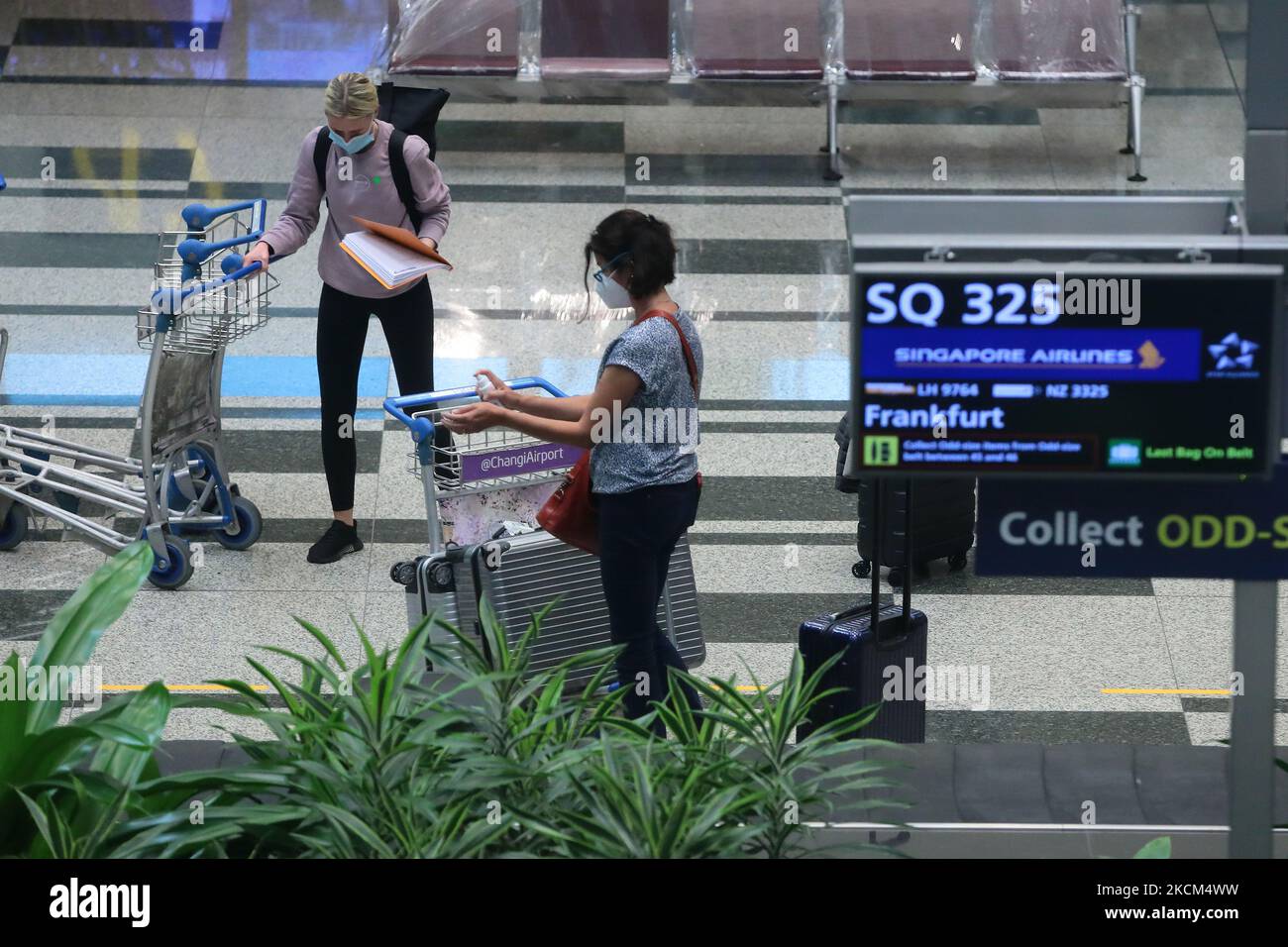 Passengers wearing protective mask collects their bags after arriving ...