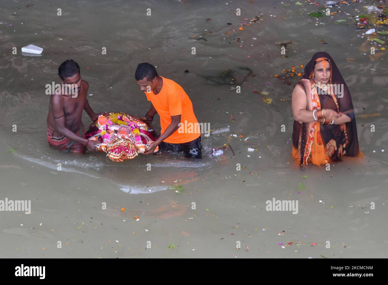 Devotees carry an idol of Ganesh for immersion as a lady prays standing ...