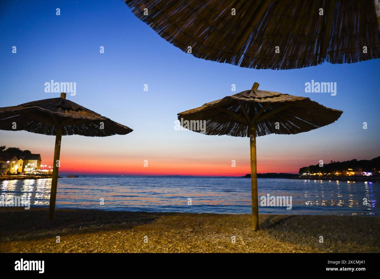Straw umbrellas are seen on a beach during a sunset in Primosten ...