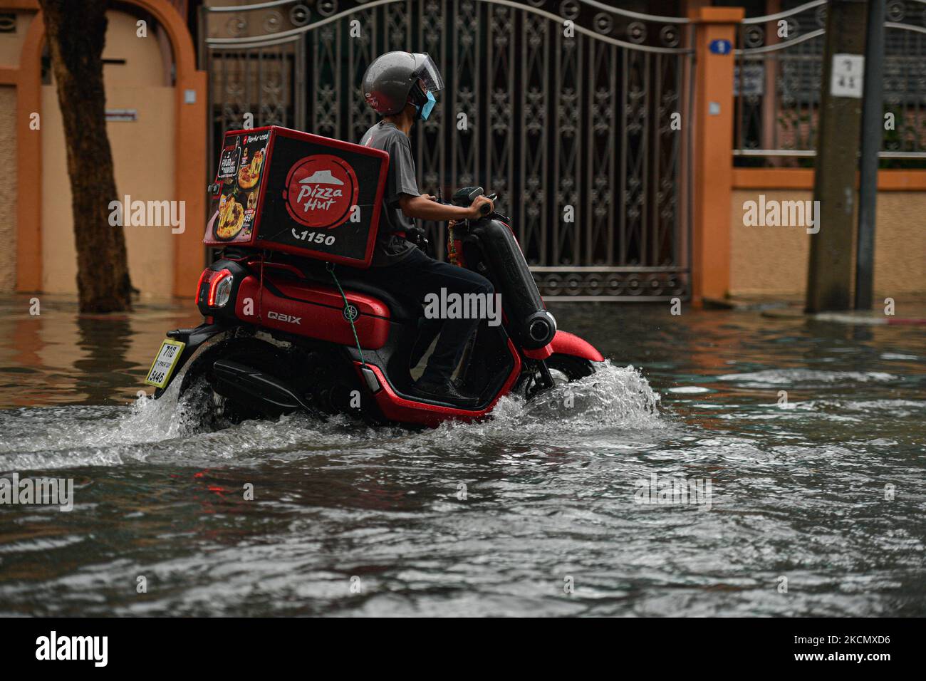 A food delivery rider rides his motorcycle through a water-logged road ...