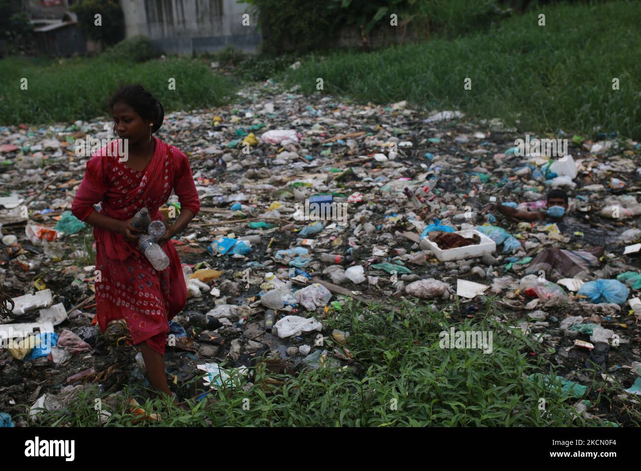 A woman collects plastic bottles from a canal to sell them to recycle ...