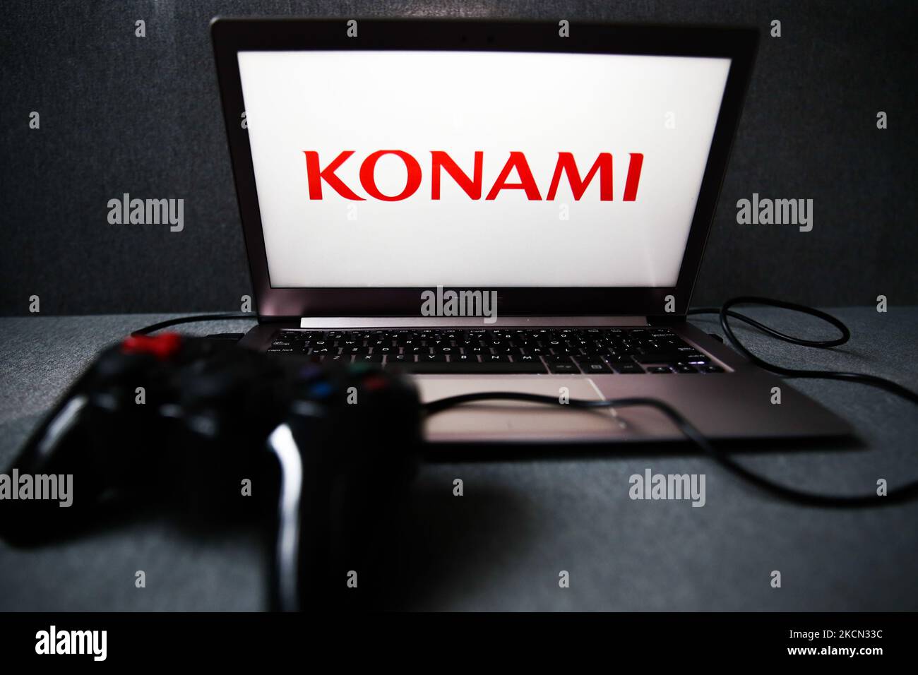 Konami logo displayed on a laptop screen and a gamepad are seen in this ...