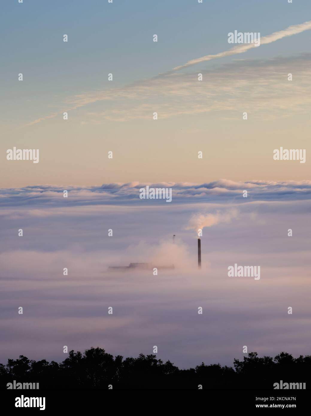 Smoke from a tall chimney drifting above the fog covered Auckland city ...