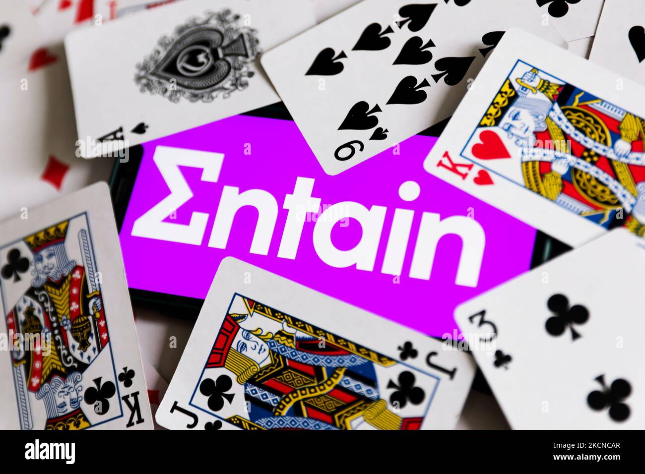 Entain logo displayed on a phone screen is seen with playing cards in ...